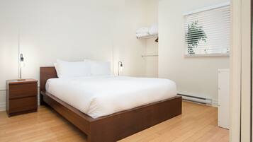Quarto com cama de madeira, mesas de cabeceira, janela com persianas e radiador.