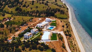Vista aérea de uma propriedade costeira com vários edifícios, piscina e praia.