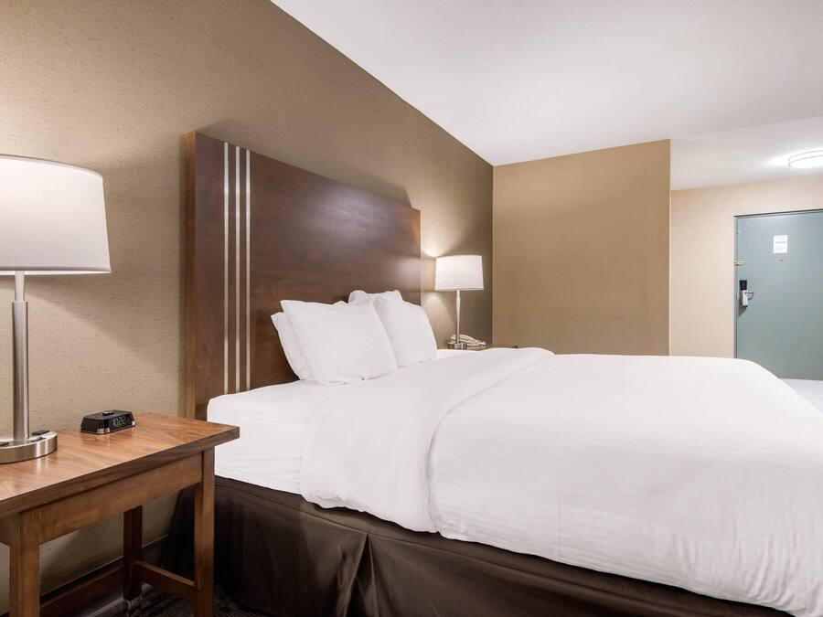 Quarto de hotel com cama, abajures, mesa de cabeceira e uma porta.