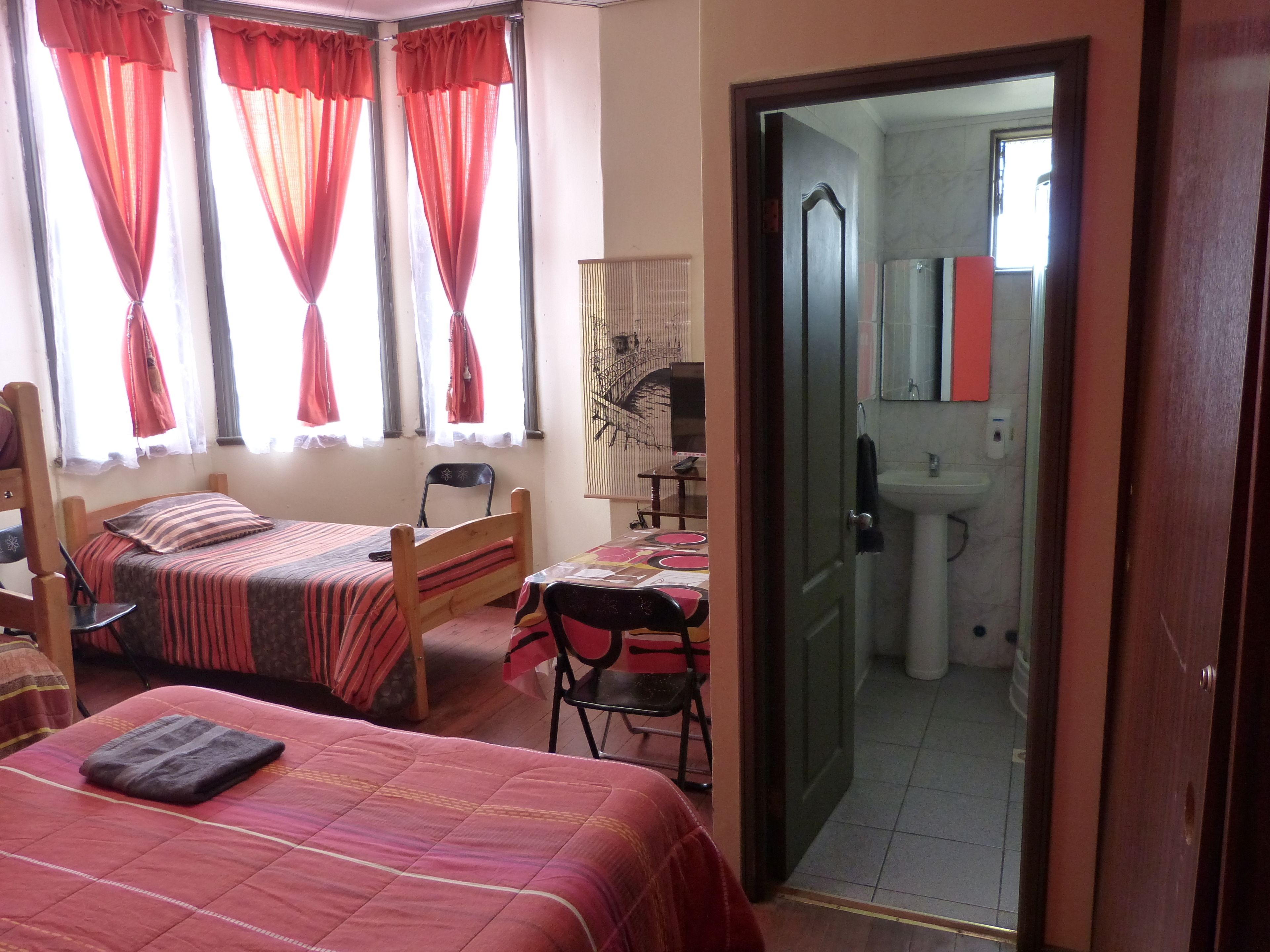Quarto com duas camas, uma escrivaninha e um banheiro visível por uma porta aberta.