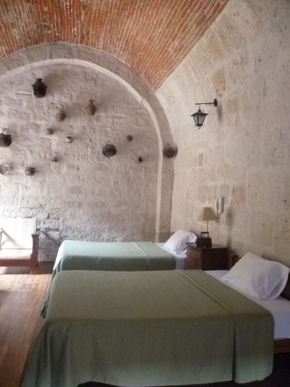 Quarto com duas camas, teto de tijolos e parede de pedra.