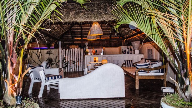 Um quarto aconchegante com decoração tropical, teto de palha, móveis de madeira e vegetação exuberante.