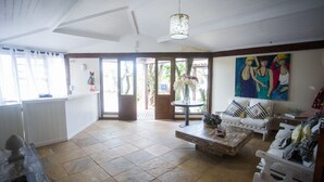 Ampla sala de estar com piso ladrilhado, sofá branco, mesa de centro e uma pintura na parede.