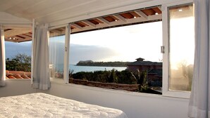 Quarto com uma cama grande, vista para o mar e varanda com vasos de terracota.