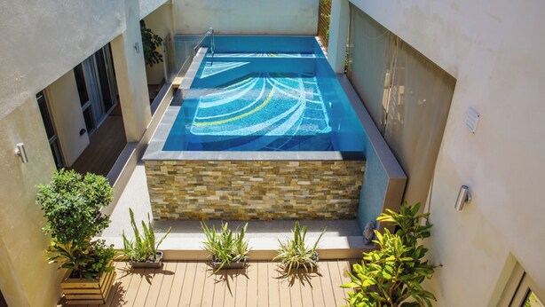 Piscina no terraço com borda de pedra, cercada por vasos de plantas.