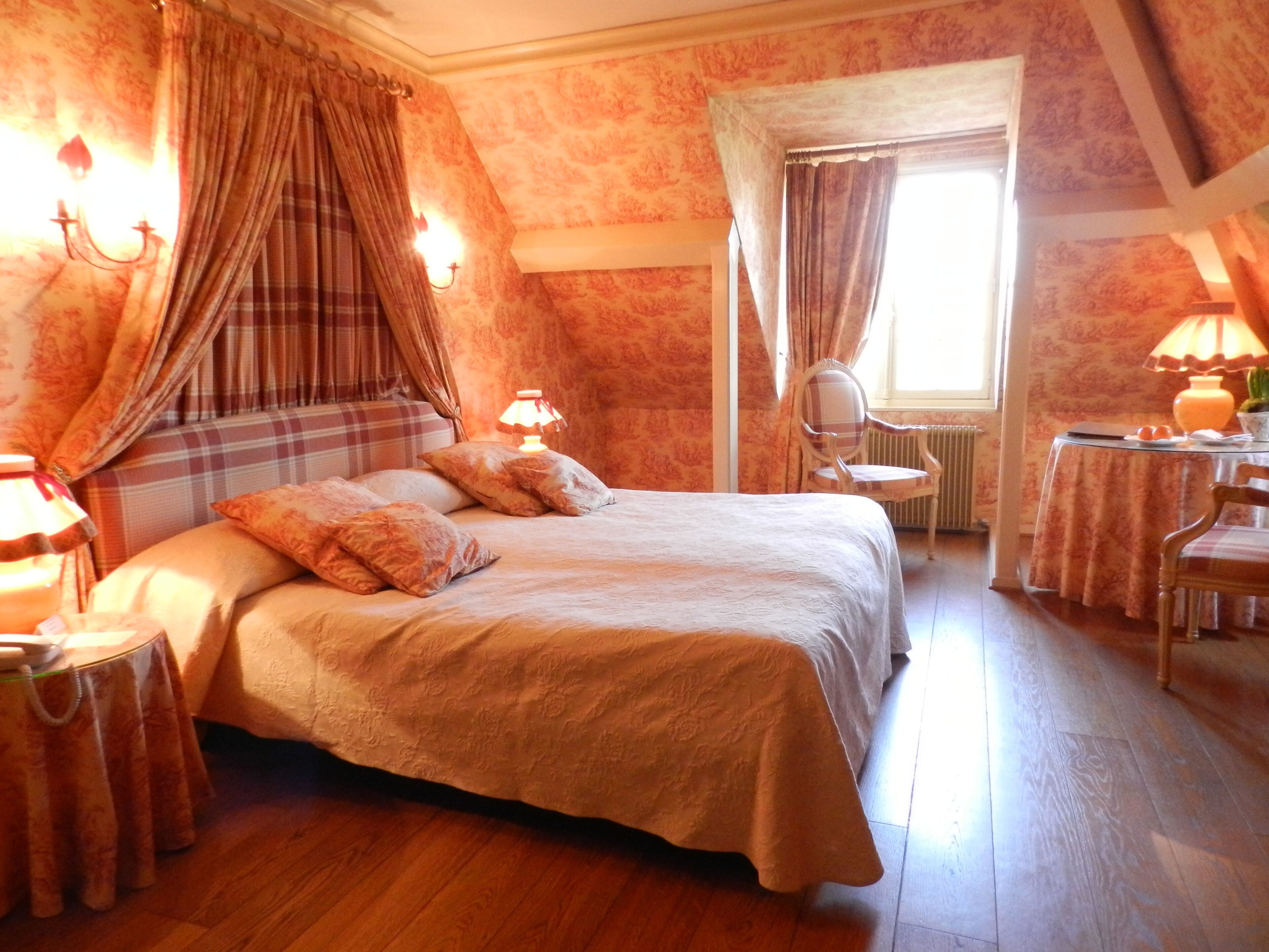 Quarto com uma cama grande, uma mesa de cabeceira, uma cadeira, uma mesa com abajur e uma janela com cortinas.