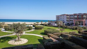 Um hotel com vista para a praia, jardins bem cuidados e céu claro.