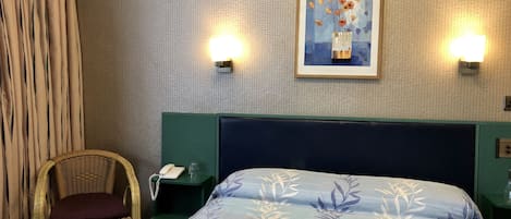 Quarto de hotel com cama, cadeira, mesa de cabeceira com telefone e um quadro na parede.