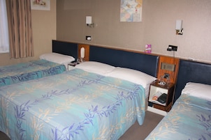 Quarto de hotel com duas camas de solteiro, uma mesa de cabeceira com abajur, uma mesinha com um lanche e um telefone fixado na parede.