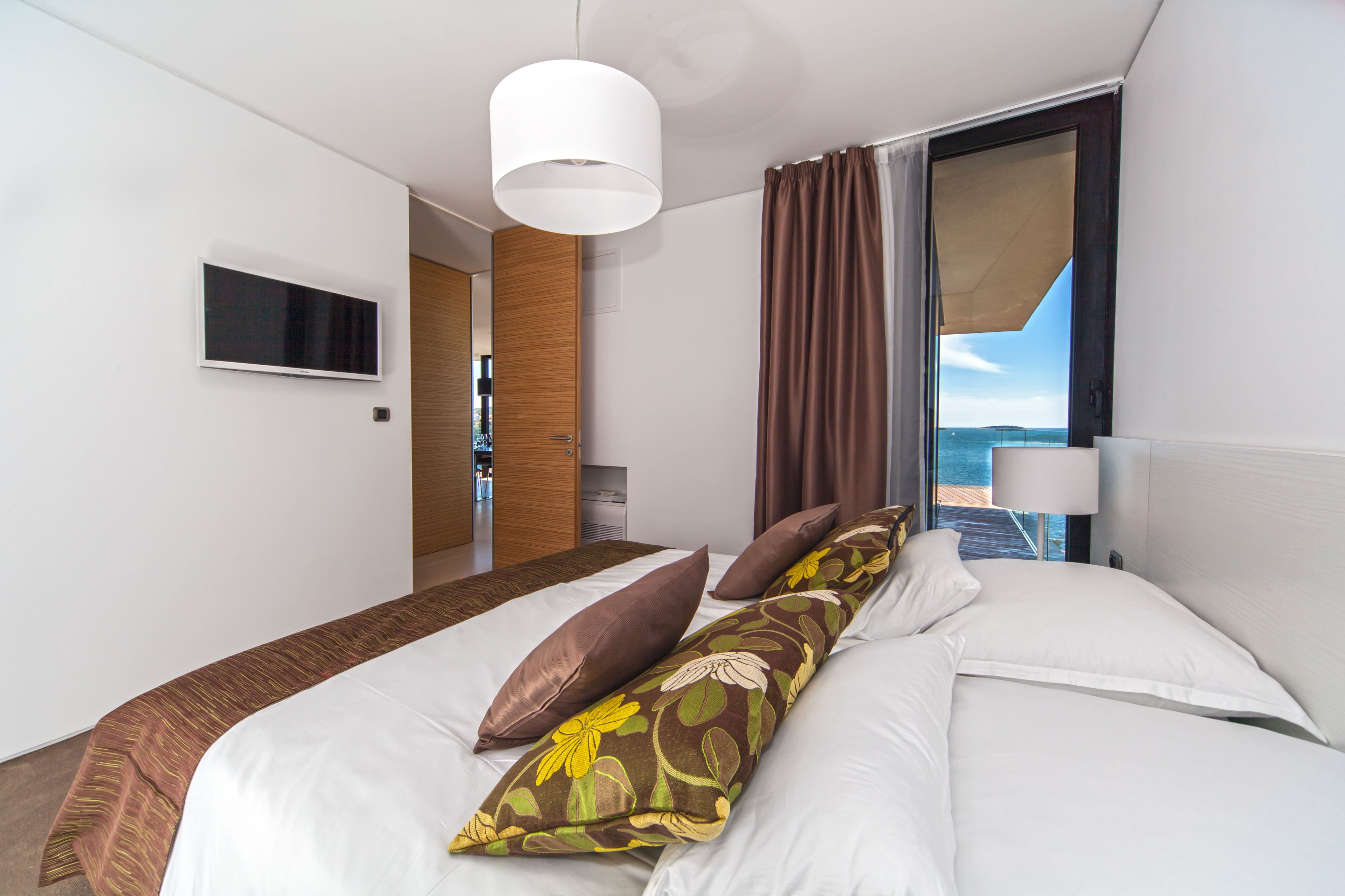 Quarto de hotel com cama, TV fixada na parede e vista para o mar pela janela.