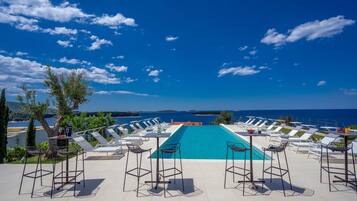 Área da piscina com espreguiçadeiras e uma mesa, com vista para um céu azul límpido e um corpo d'água.