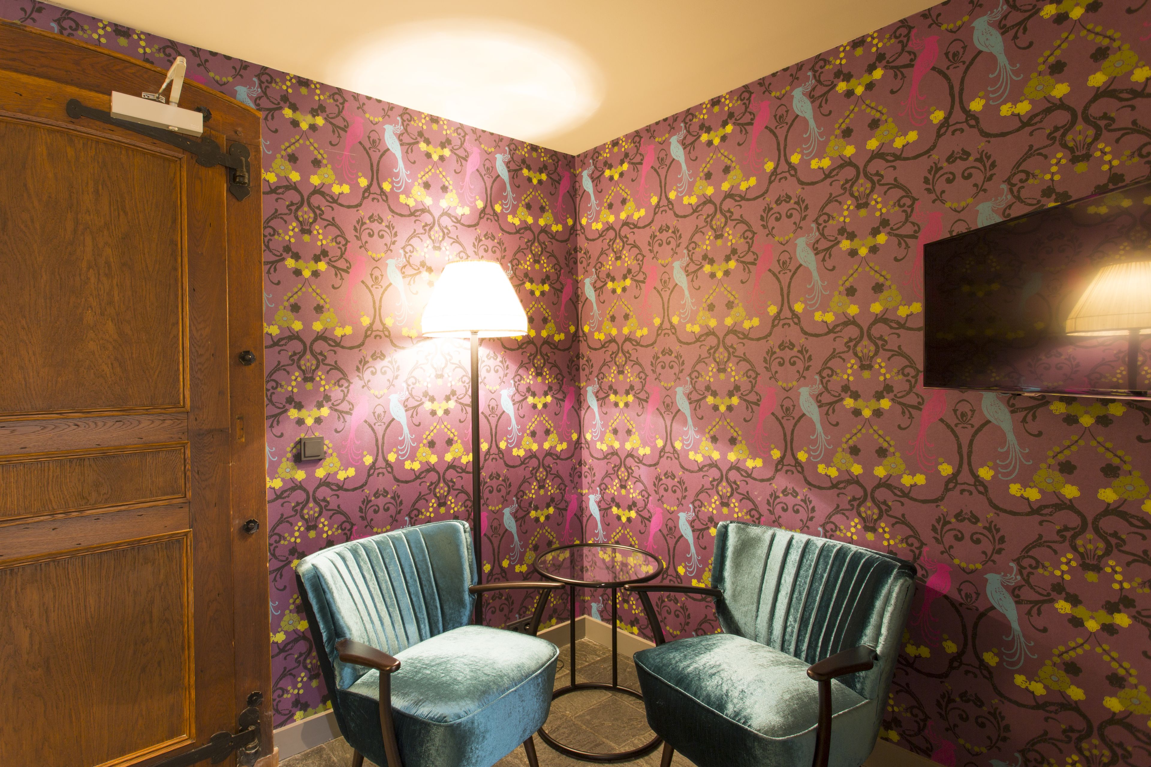 Um quarto com duas poltronas estofadas azuis, uma mesa redonda, uma porta de madeira e uma parede com padrão floral.