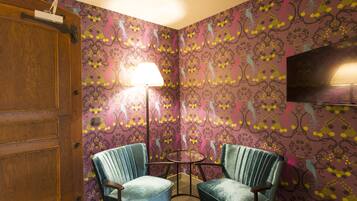 Um quarto com duas poltronas estofadas azuis, uma mesa redonda, uma porta de madeira e uma parede com padrão floral.