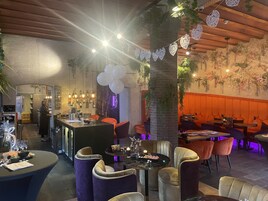 Um restaurante com mesas redondas, cadeiras estofadas e luminárias pendentes.