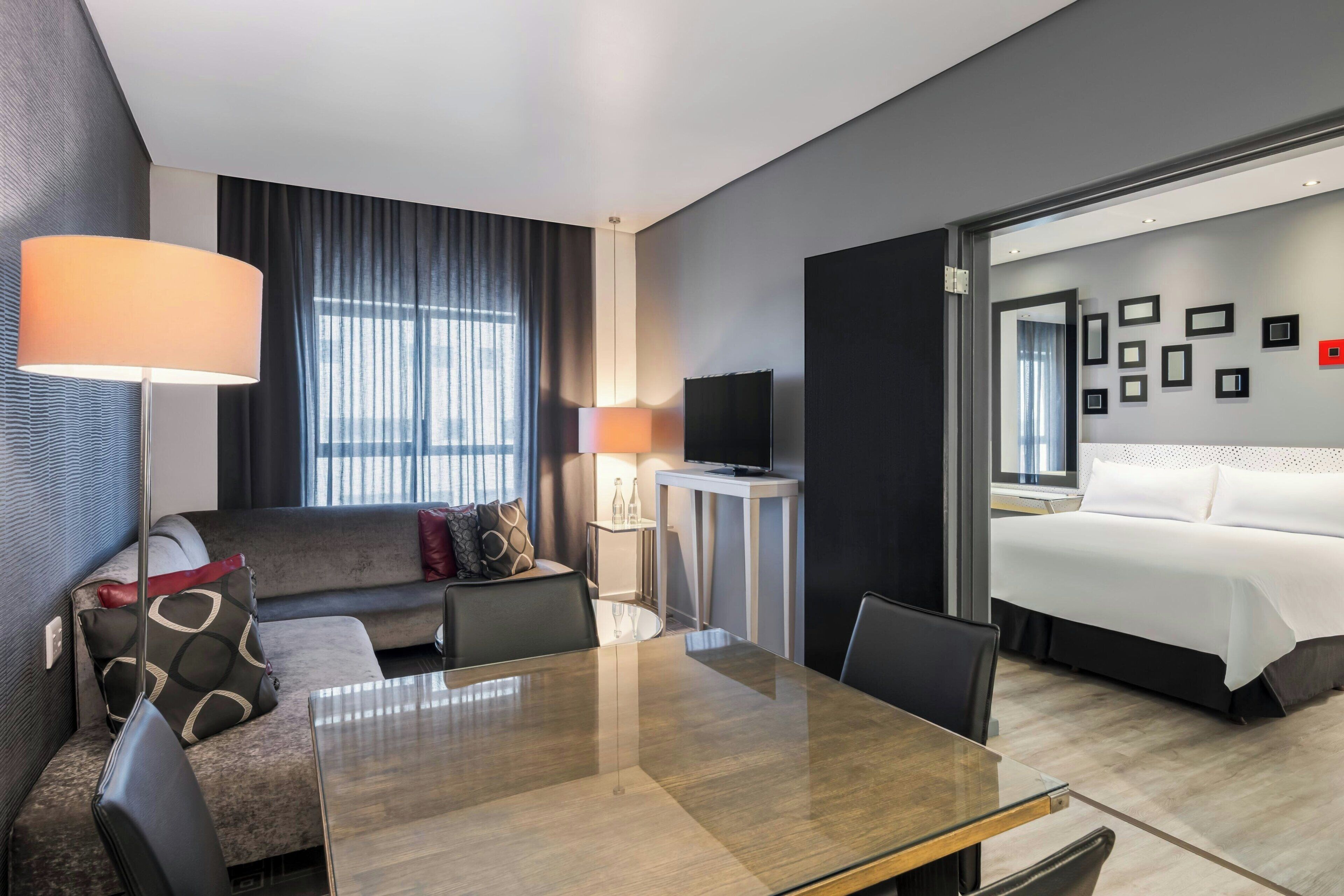 Quarto de hotel moderno com sofá, mesa de jantar, televisão e cama.