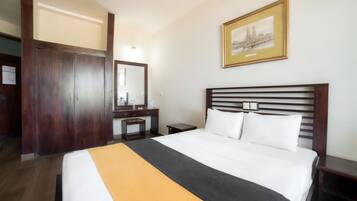 Quarto de hotel com cama grande, guarda-roupa de madeira, mesa de cabeceira e um quadro na parede.