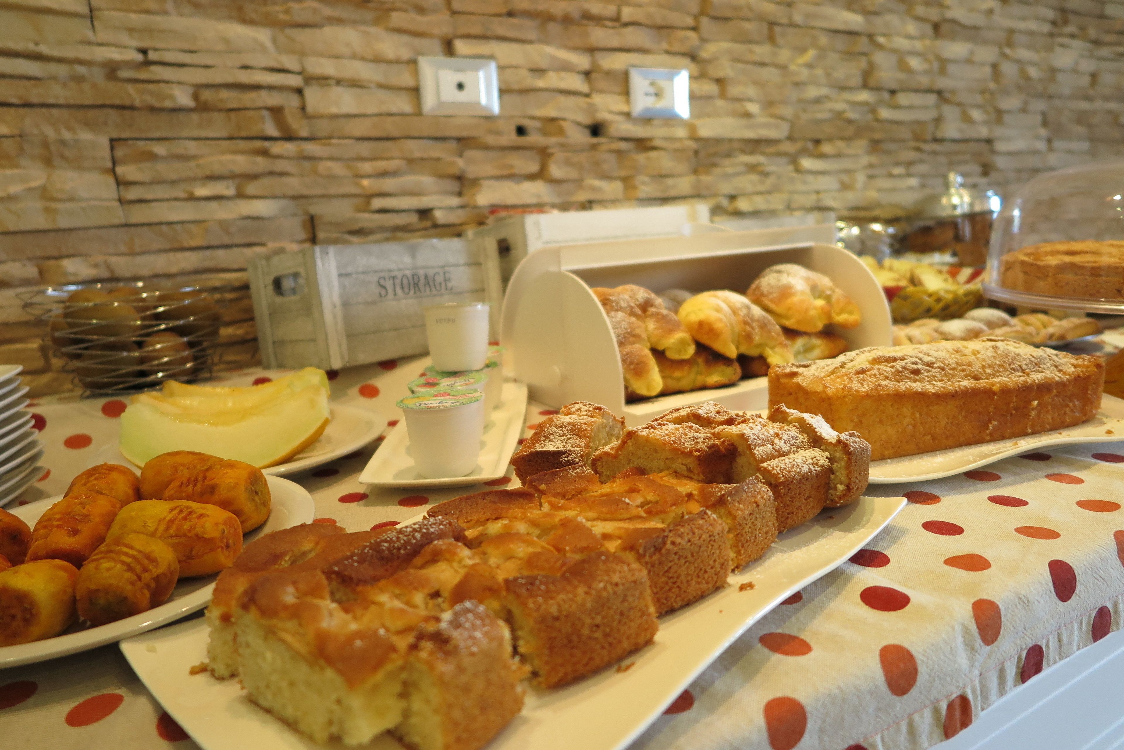 Uma mesa de buffet com diversos produtos de panificação, incluindo pão, doces e um bolo.