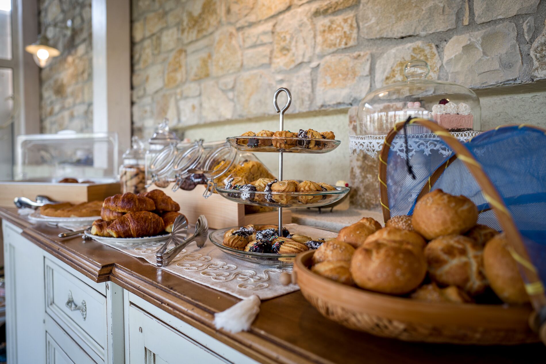 Buffet com diversos doces e produtos de pastelaria expostos num balcão, com um fundo de parede de pedra.