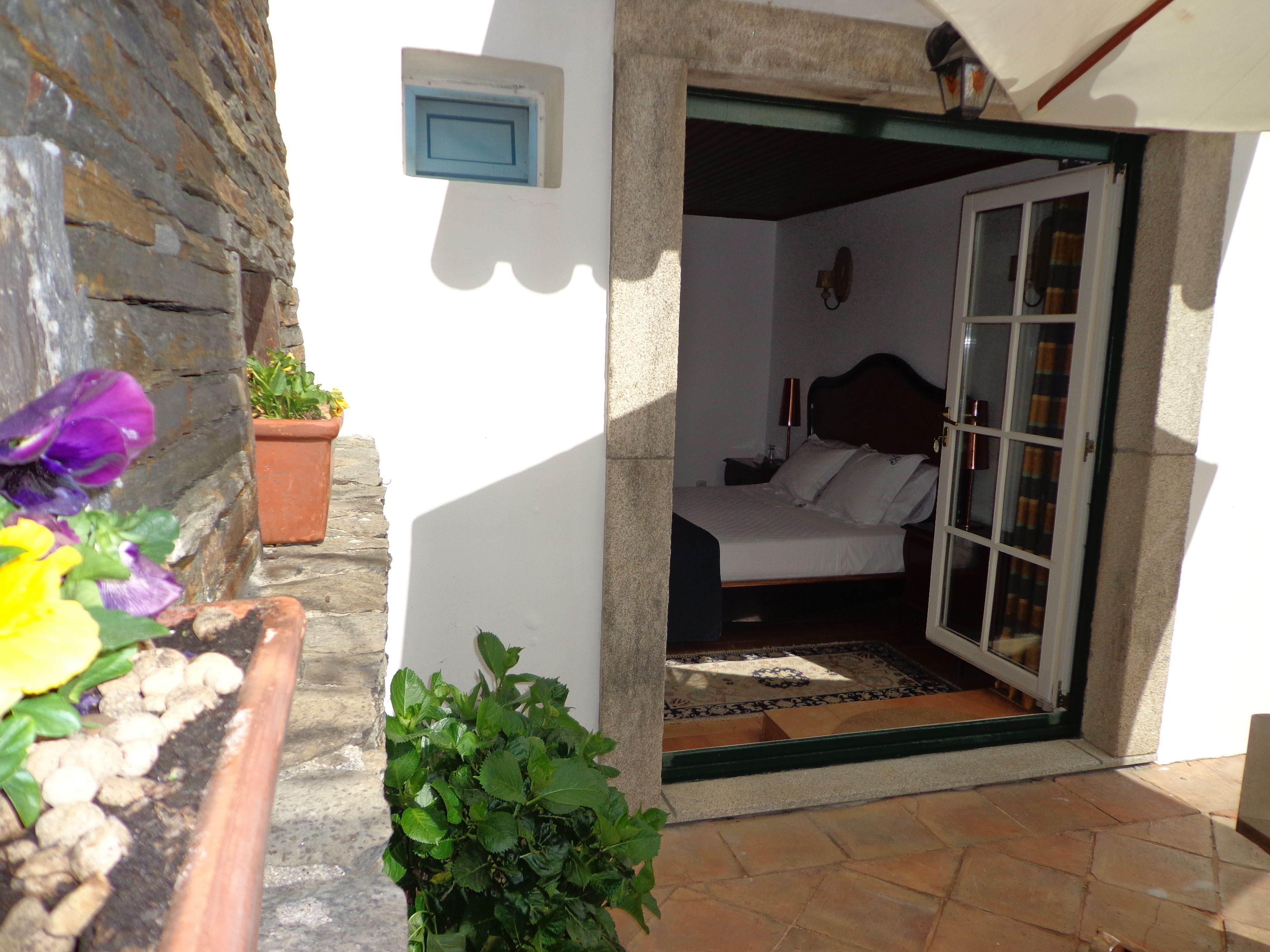 Quarto com uma cama, uma pequena janela e uma porta que dá para o exterior.