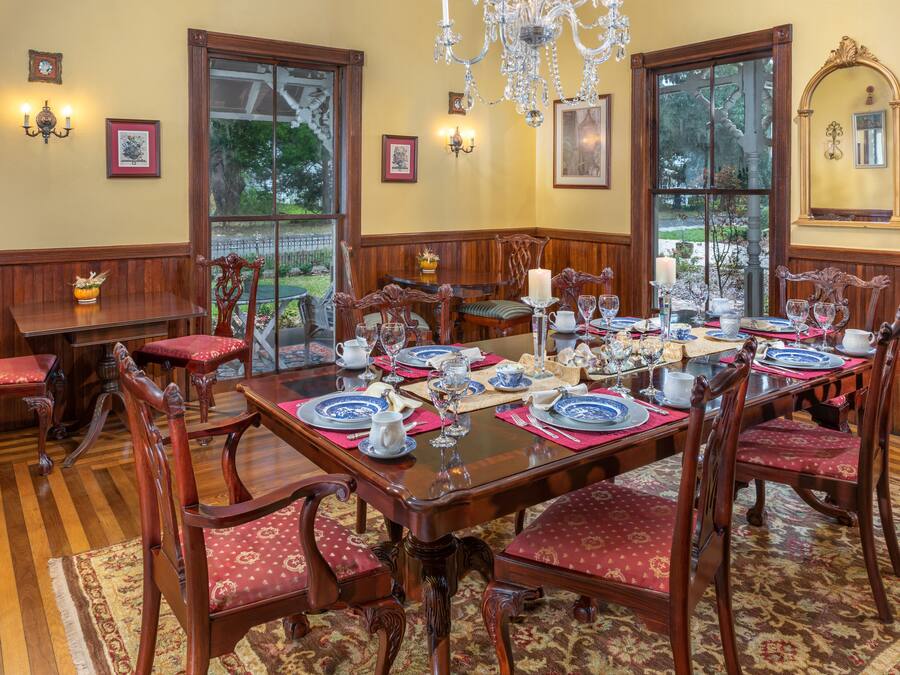 Uma sala de jantar formal com uma grande mesa de madeira posta para seis pessoas, cercada por cadeiras ornamentadas.