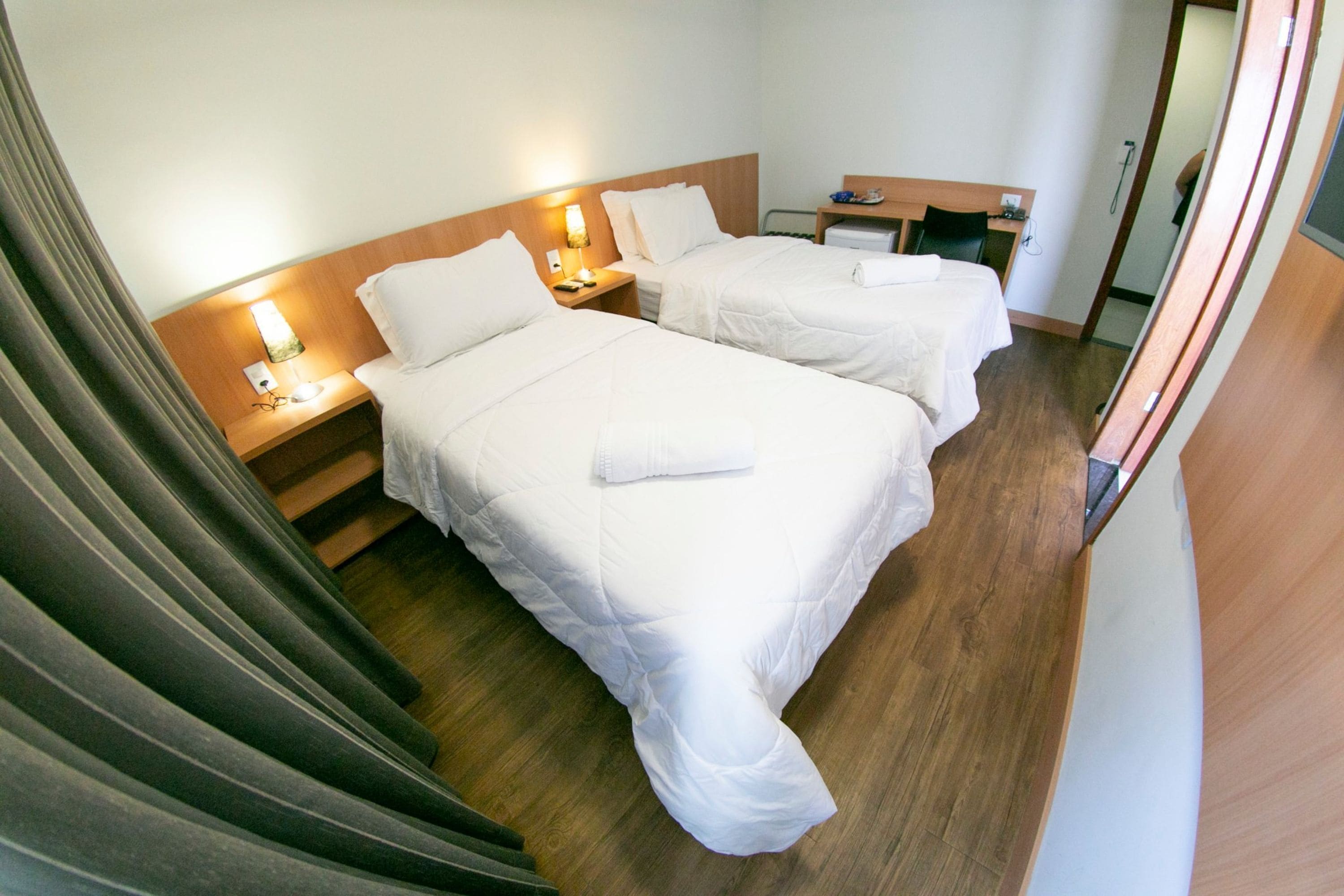 Quarto de hotel com duas camas, uma escrivaninha e um espelho.