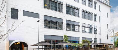 Um edifício moderno de vários andares com fachada branca, janelas amplas e áreas de estar ao ar livre com guarda-sóis.