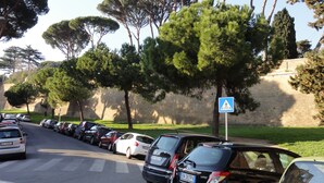 Um parque de estacionamento com carros estacionados ao longo de uma rua arborizada e com uma parede de pedra.