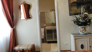 Um quarto com uma cama, cômoda, espelho, mala e um quadro na parede.