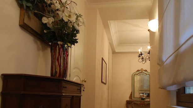 Um corredor com piso de madeira, um armário de madeira com um vaso de flores, um espelho e um luminário.