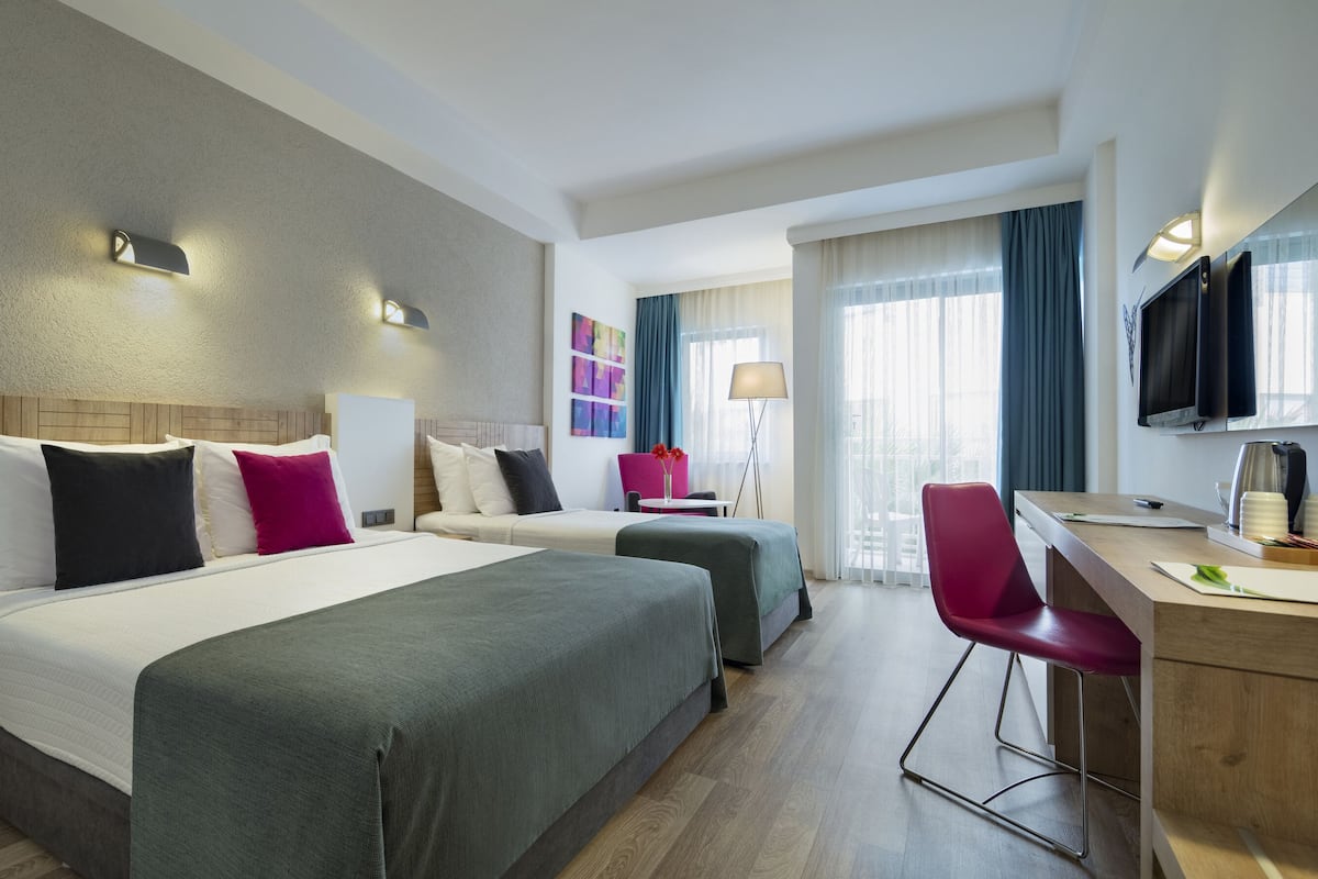 Quarto de hotel com duas camas, uma escrivaninha, uma cadeira, uma televisão e um abajur.