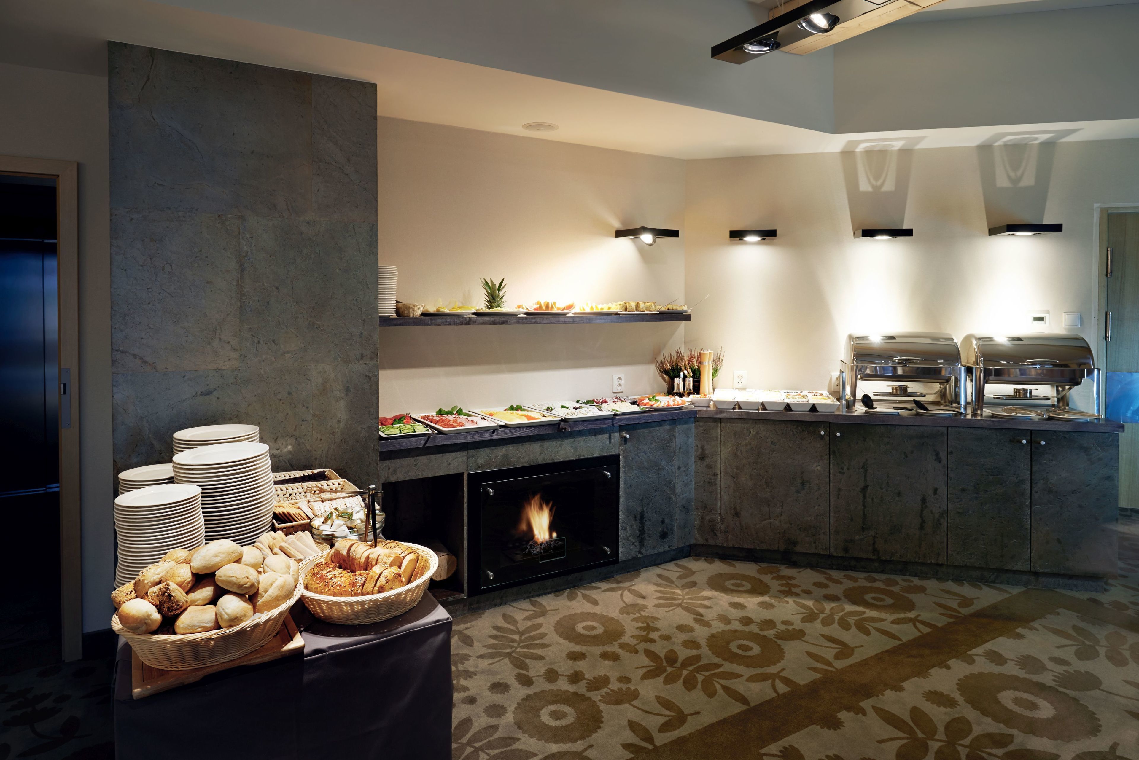 Uma mesa de buffet com diversos alimentos, uma lareira e estações de buffet.