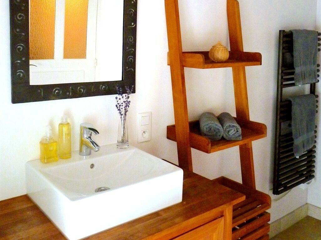 Casa de banho com lavatório branco, estante de madeira com toalhas e espelho com moldura preta.