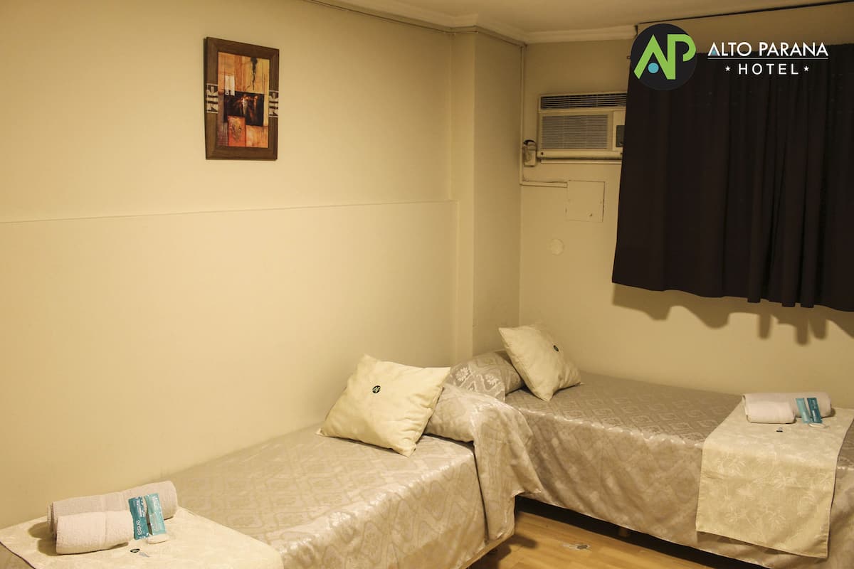 Quarto de hotel com duas camas de solteiro, ar condicionado fixado na parede e um quadro emoldurado.