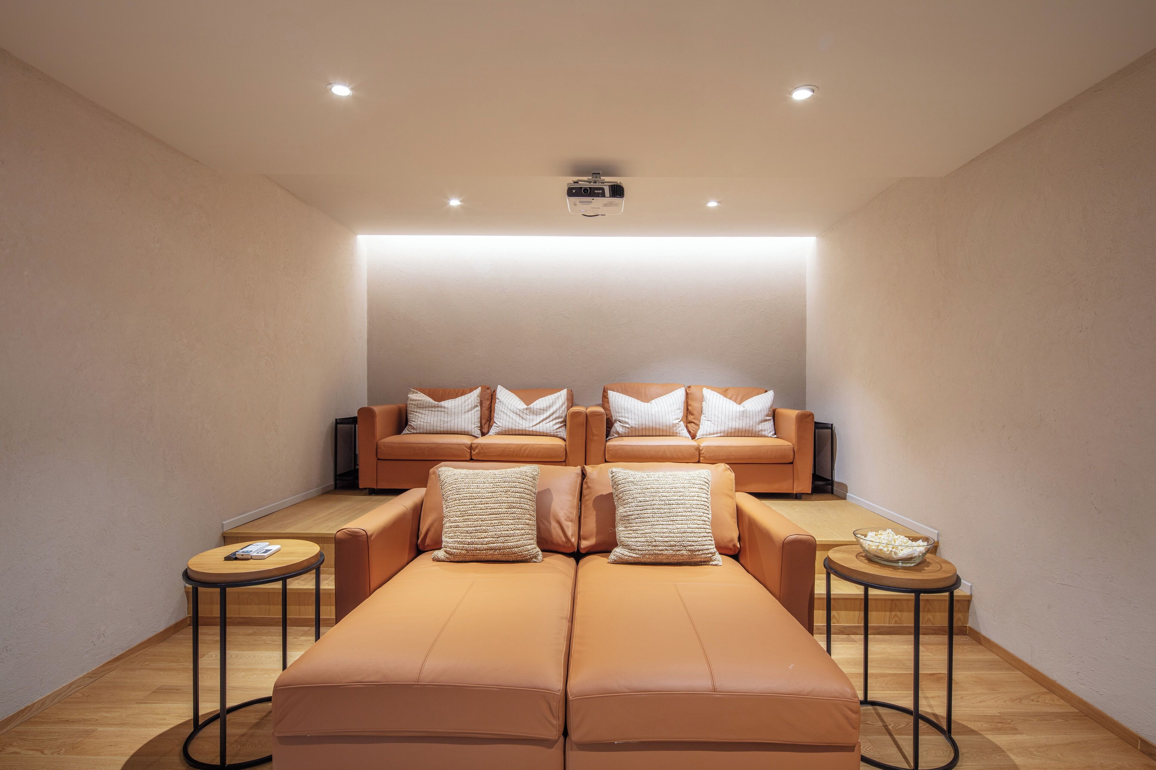 Quarto moderno com sofá, duas mesinhas laterais, projetor no teto e iluminação embutida.