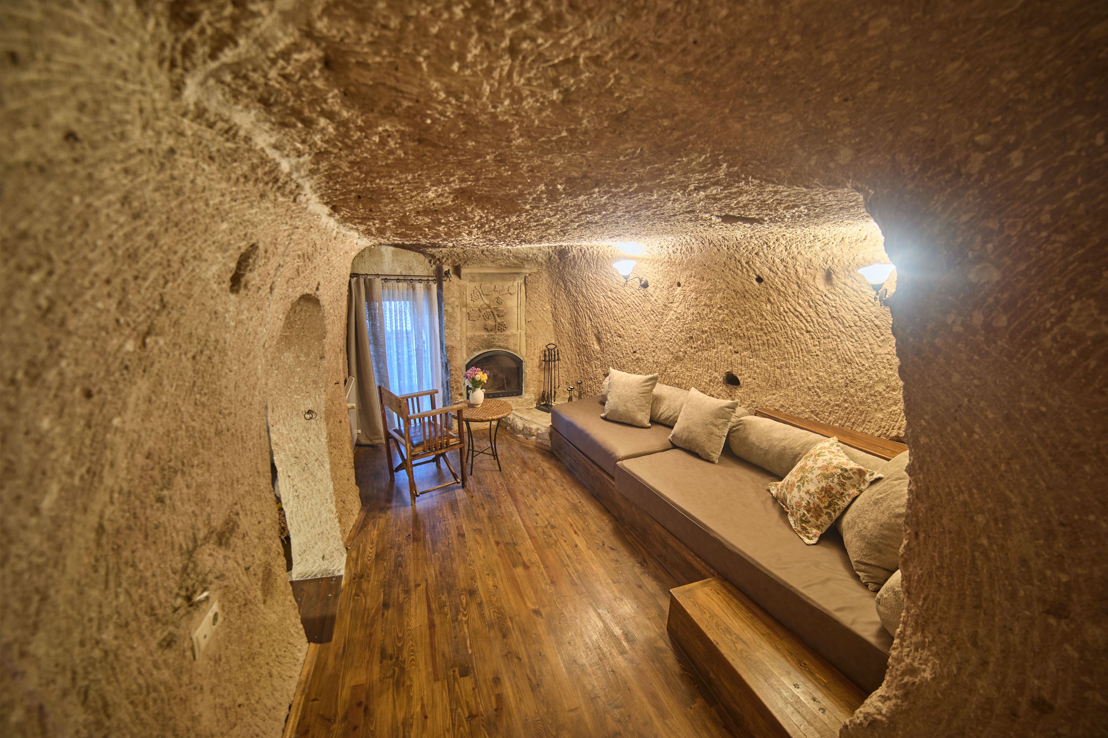 Um interior rústico com parede de pedra, assoalho de madeira, um sofá, uma poltrona e uma lareira.