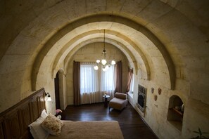 Quarto com teto abobadado, cama, poltrona, mesinha e lustre.