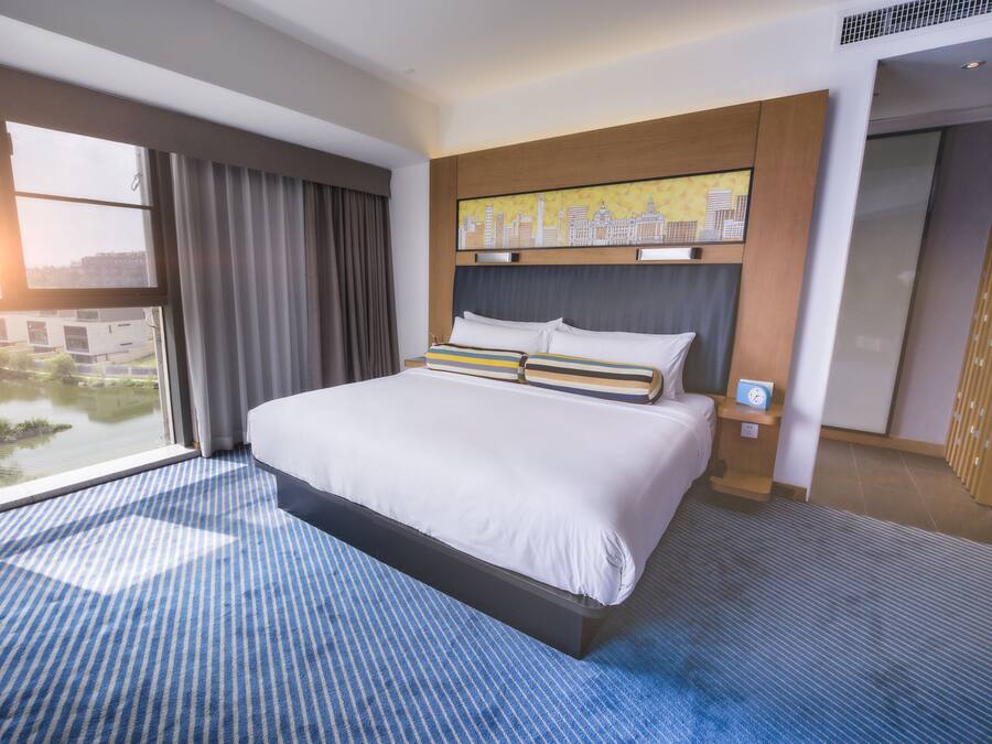 Quarto de hotel com uma cama grande, vista da cidade pela janela e uma obra de arte com o horizonte urbano na parede.