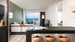 Quarto de hotel moderno com varanda, área de refeições com mesa e cadeiras, e vista para o mar.