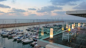 Marina com barcos atracados, um deck de madeira com área de estar externa e uma barreira de vidro com vista para a água.