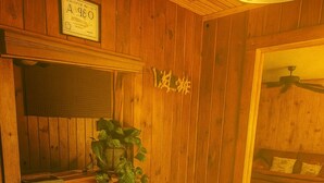 Um quarto de madeira com teto de madeira, um ventilador de teto, uma janela com persianas, uma planta e uma porta.
