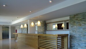 Uma área de recepção moderna com balcão de madeira, parede de pedra e luminárias pendentes.