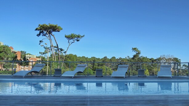 Área de piscina com espreguiçadeiras e céu claro.