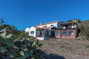 Um edifício branco com telhado de telhas vermelhas, uma parede de pedra e uma planta cacto em primeiro plano.