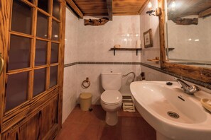 Casa de banho com porta de madeira, sanita, lavatório e espelho.