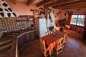 Uma cozinha rústica com painel de azulejos, armários de madeira, fogão a gás e um espaço de refeições com mesa e cadeiras.