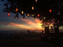 Vista do pôr do sol com praia e árvore com lanternas penduradas.