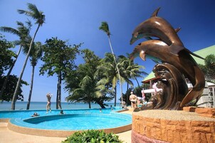Uma piscina com uma escultura de golfinho, rodeada por palmeiras e vista para o oceano.