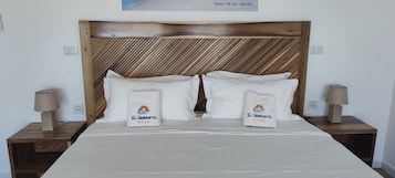Cama bem arrumada com duas almofadas e duas toalhas, cada uma com o logotipo "El Quenamo".
