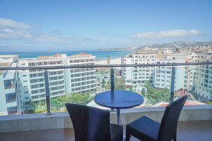 Uma varanda com mesa e cadeiras, com vista para a paisagem urbana e o mar.