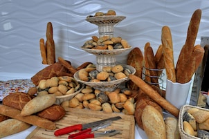 Diversos pães e folhados expostos em uma mesa com tábua de corte e utensílios.